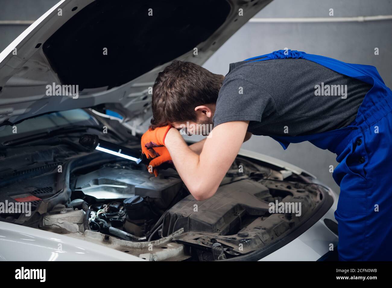 A man in overalls inspects a car engine using a lamp Stock Photo - Alamy