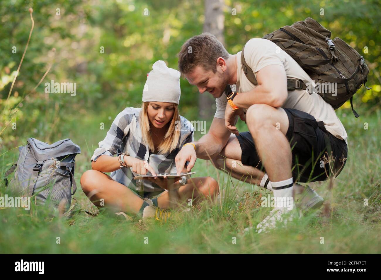 Young hikers sitting on the ground looking at an old map with a compass ...