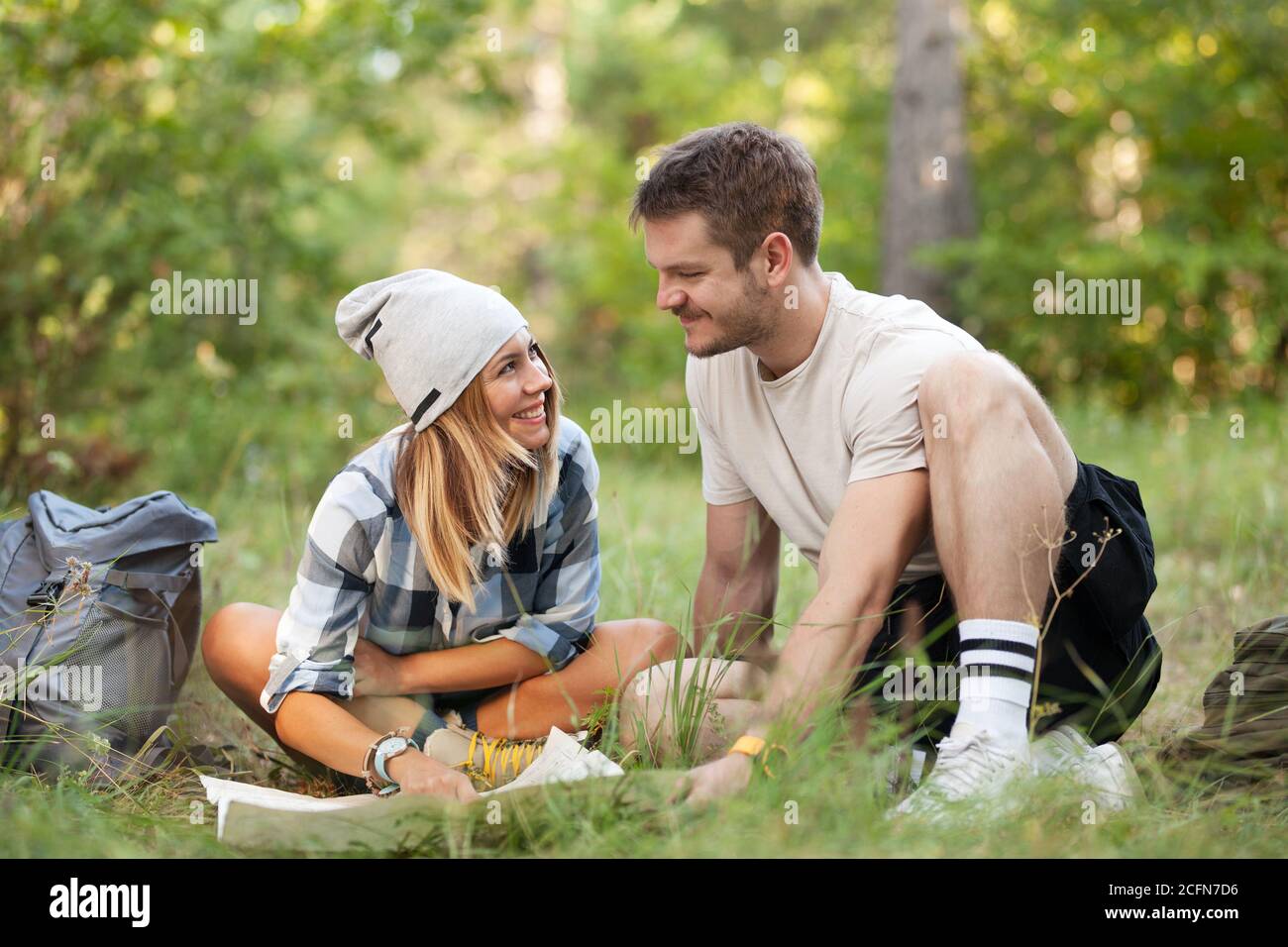 Young hikers sitting on the ground looking at an old map with a compass ...