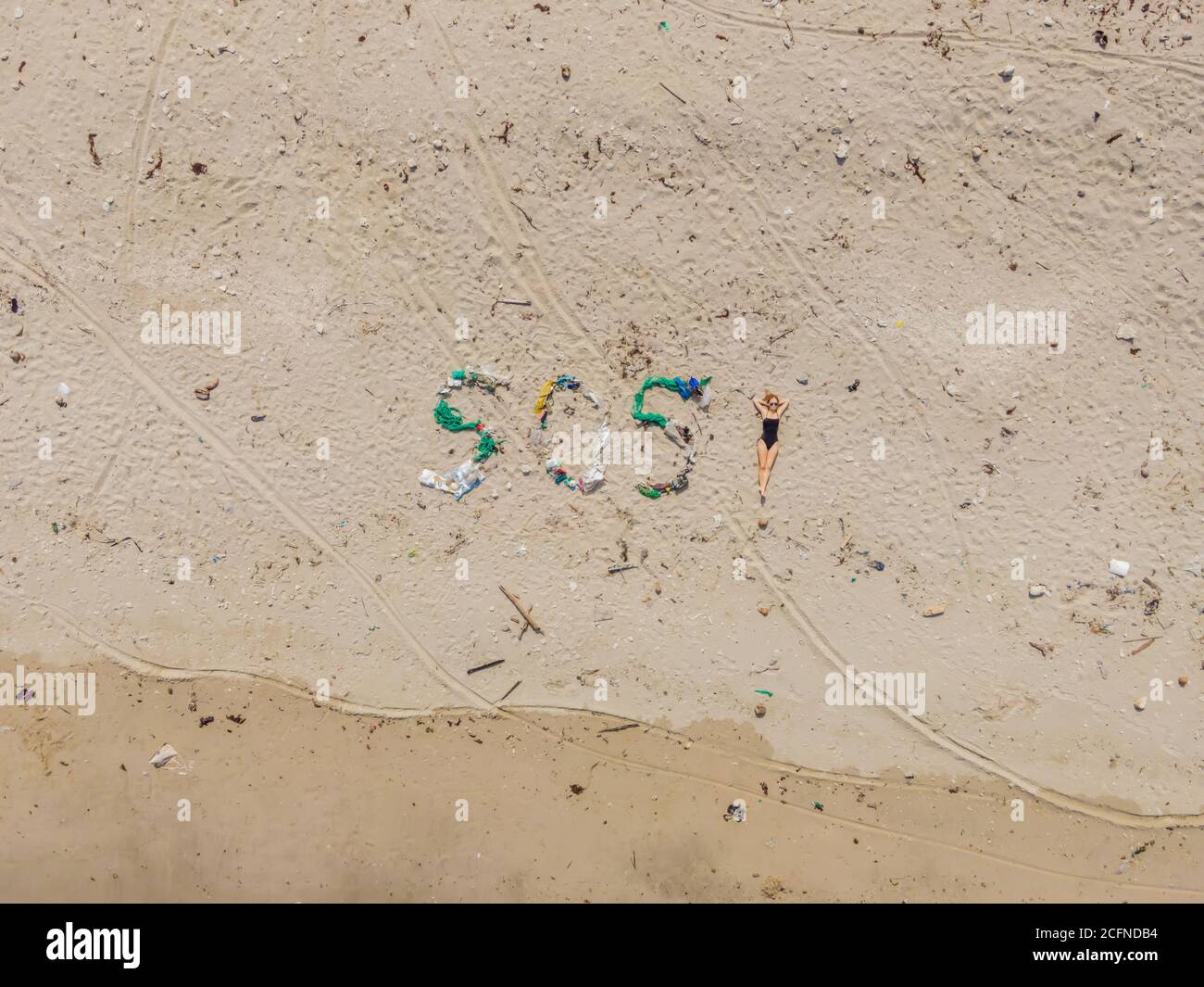 SOS inscription and woman sunbathes on the beach nearby. Environmental ...