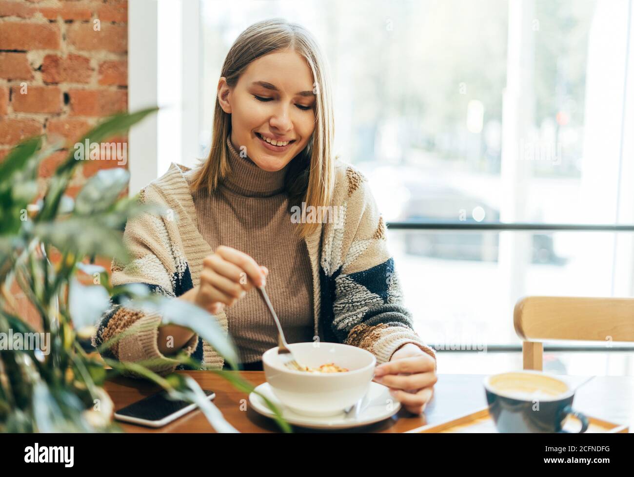Young smiling blonde woman in casual clothing having lunch at the cafe ...