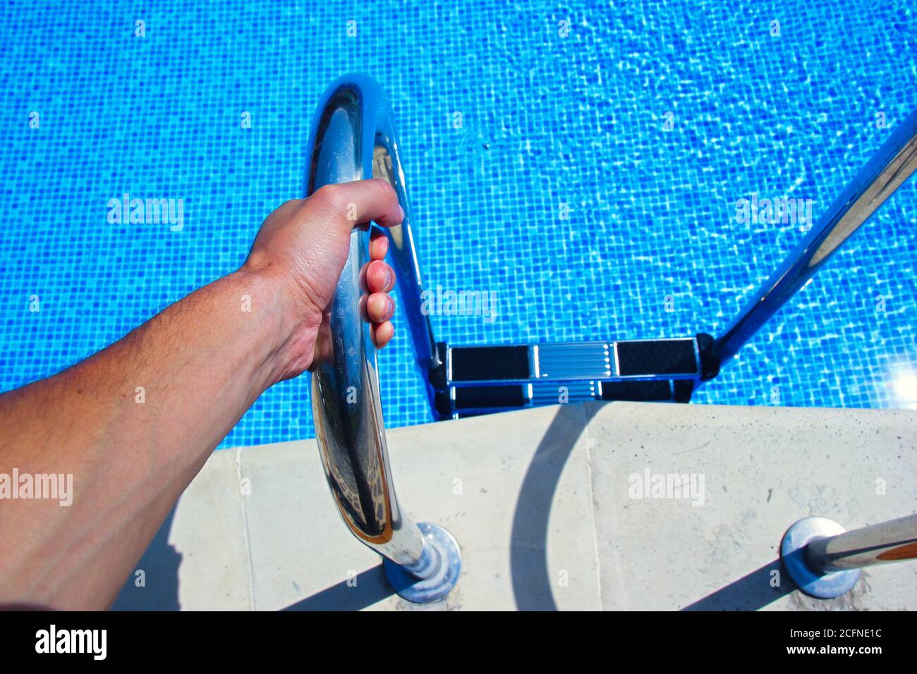 Stairs to the pool filled with clean water. Hand holds the handrail ...