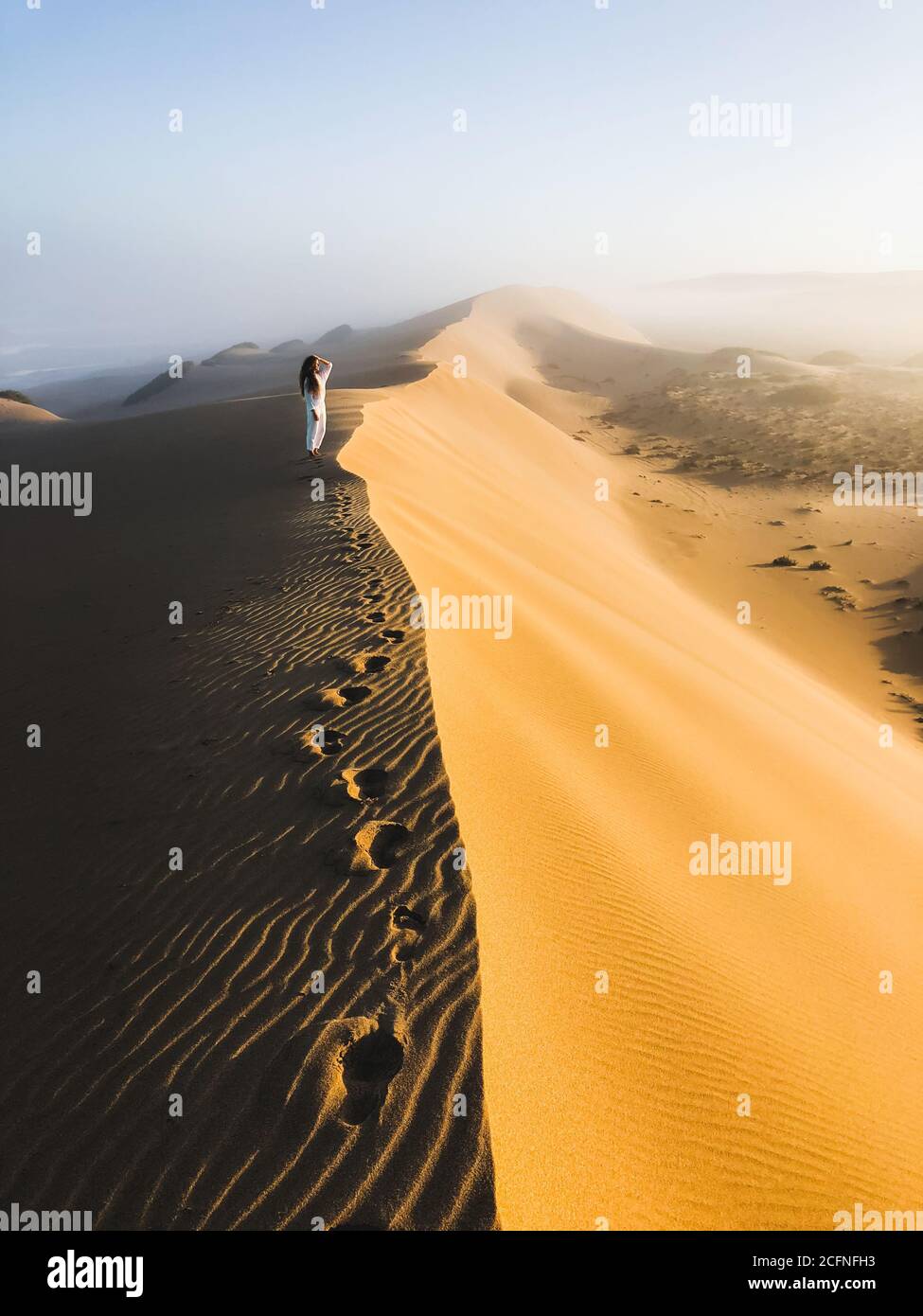 Woman enjoying sunrise on top of huge sand dune. Beautiful warm sun ...
