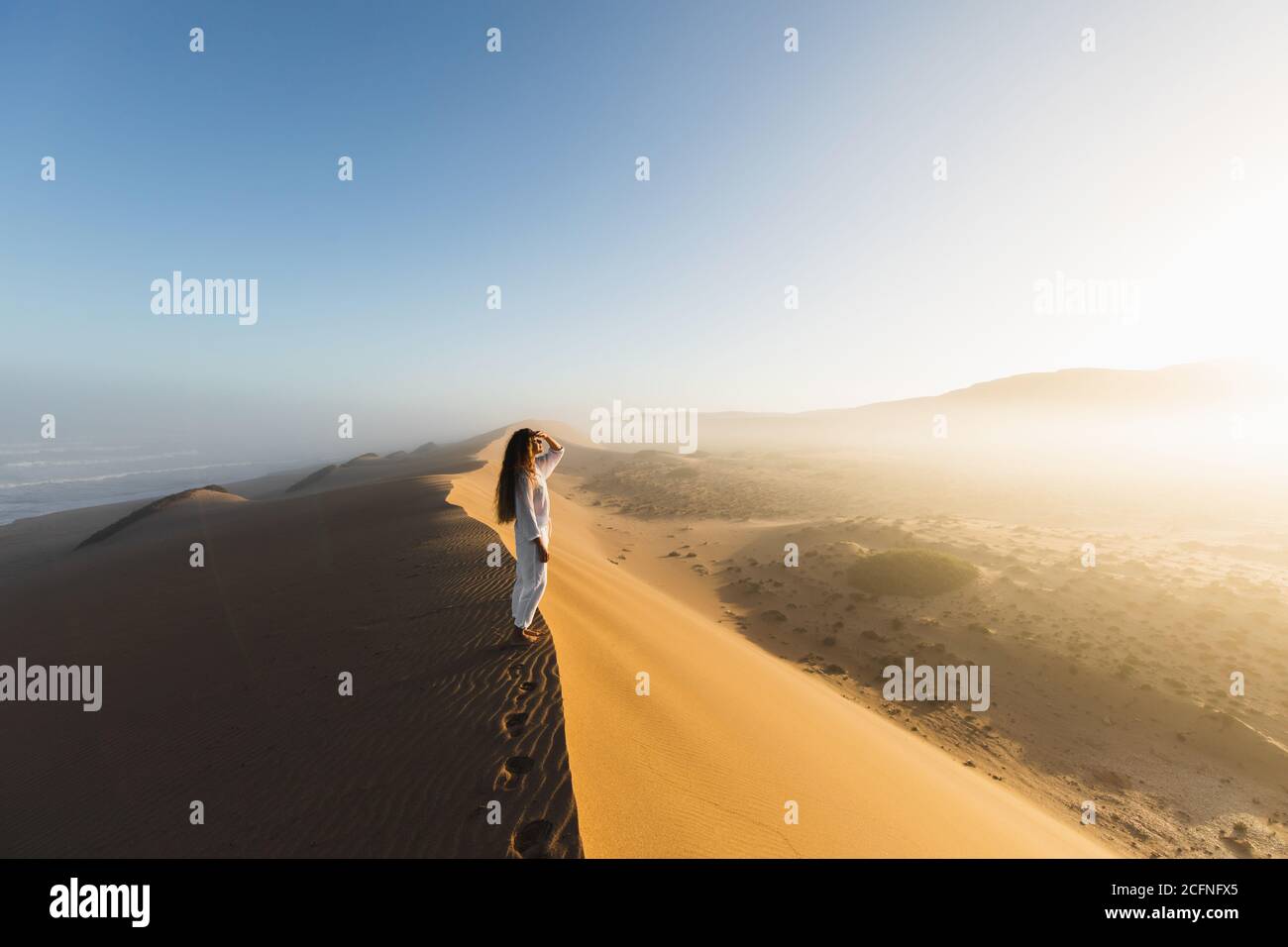 Woman enjoying sunrise on top of huge sand dune. Beautiful warm sun ...