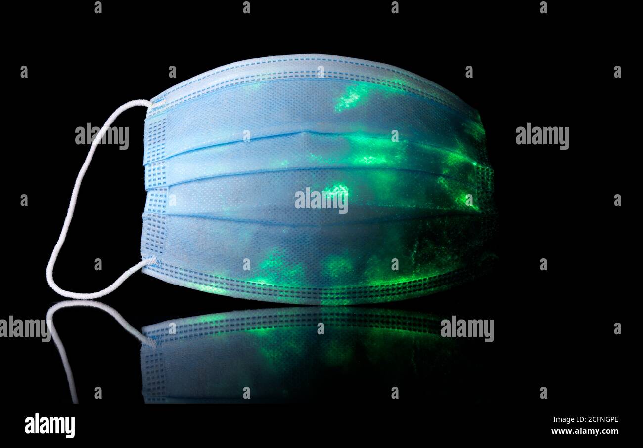 Contaminated medical face mask with glowing green spots representing ...