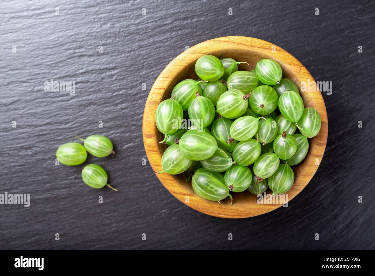 Fresh gooseberries in wooden bowl on black stone slate background. Top ...
