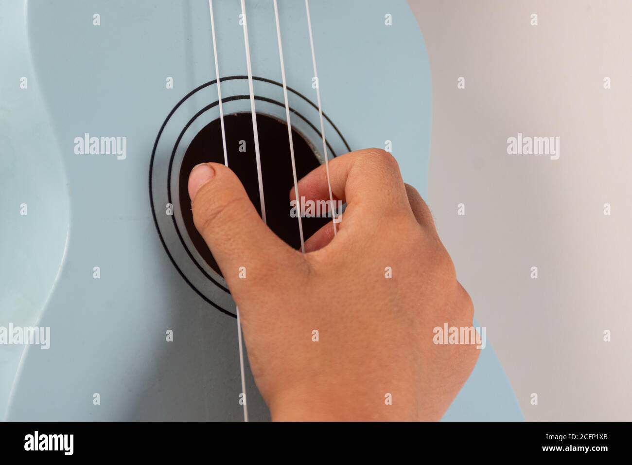 Close up of a modern ukulele played by a hand on a neutral background ...