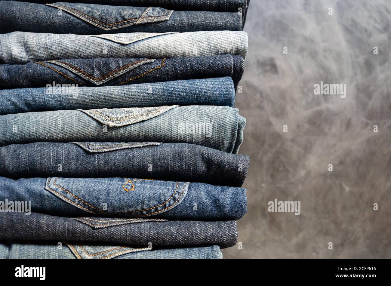 A stack of neatly folded jeans on gray background. Close-up of jeans in ...