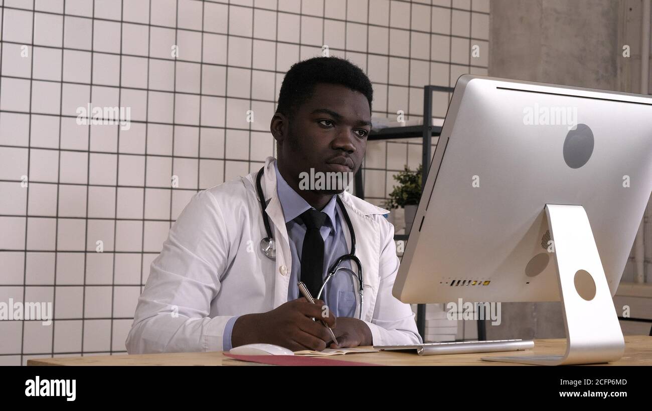 Young african-american doctor making notes and looking up something on ...