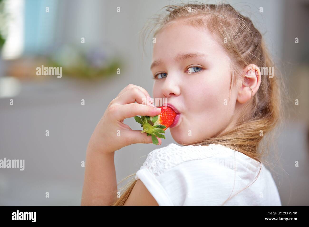 Blonde girl eating strawberry in the kitchen Stock Photo - Alamy