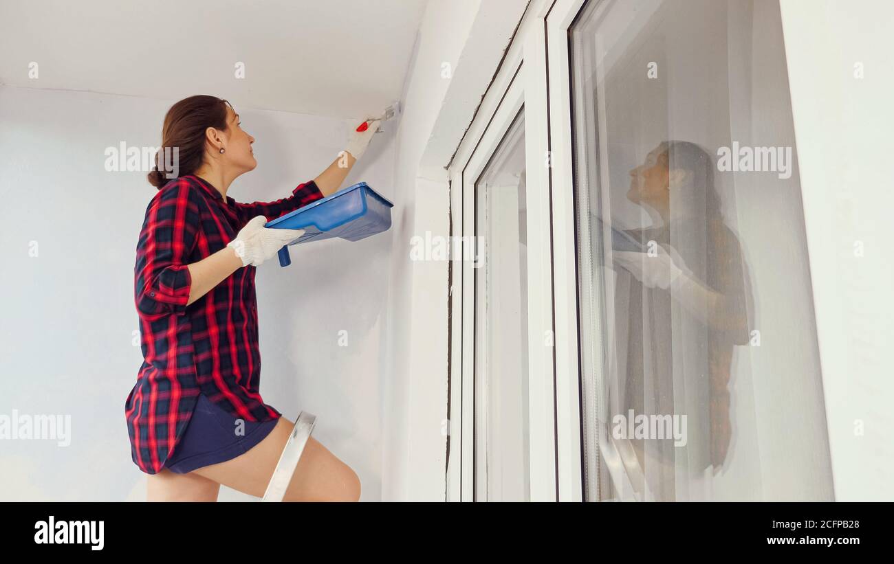 young woman in shorts and red checkered shirt goes up step ladder with ...