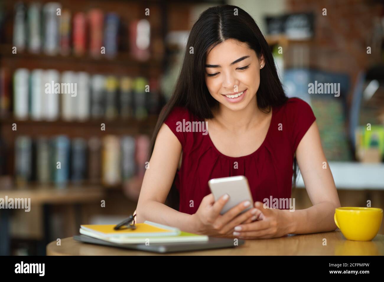 Smiling Asian Woman Texting On Smartphone While Having Coffee Break In ...