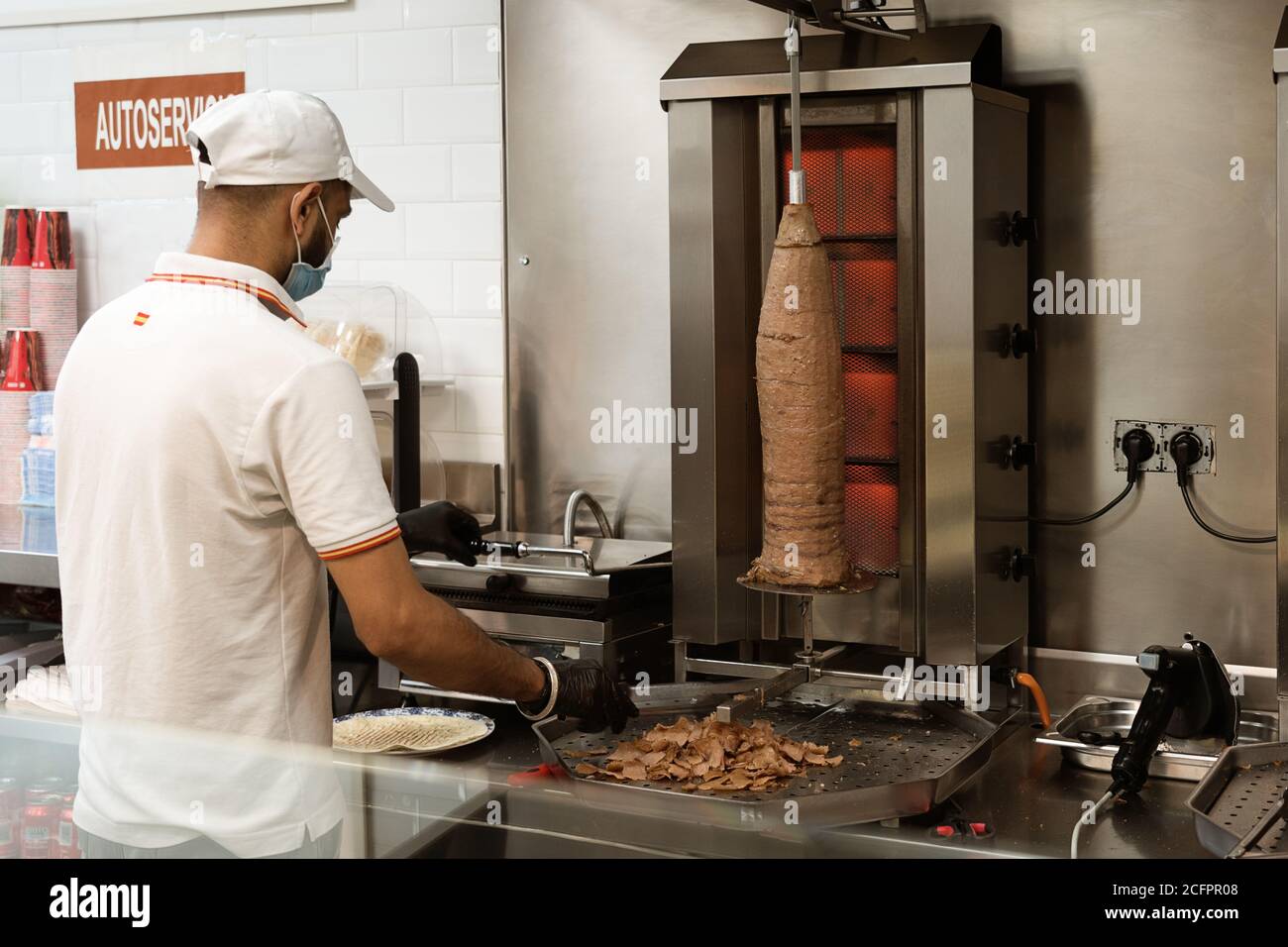 Uniformed chef, cutting and preparing chicken and beef doner kebabs ...