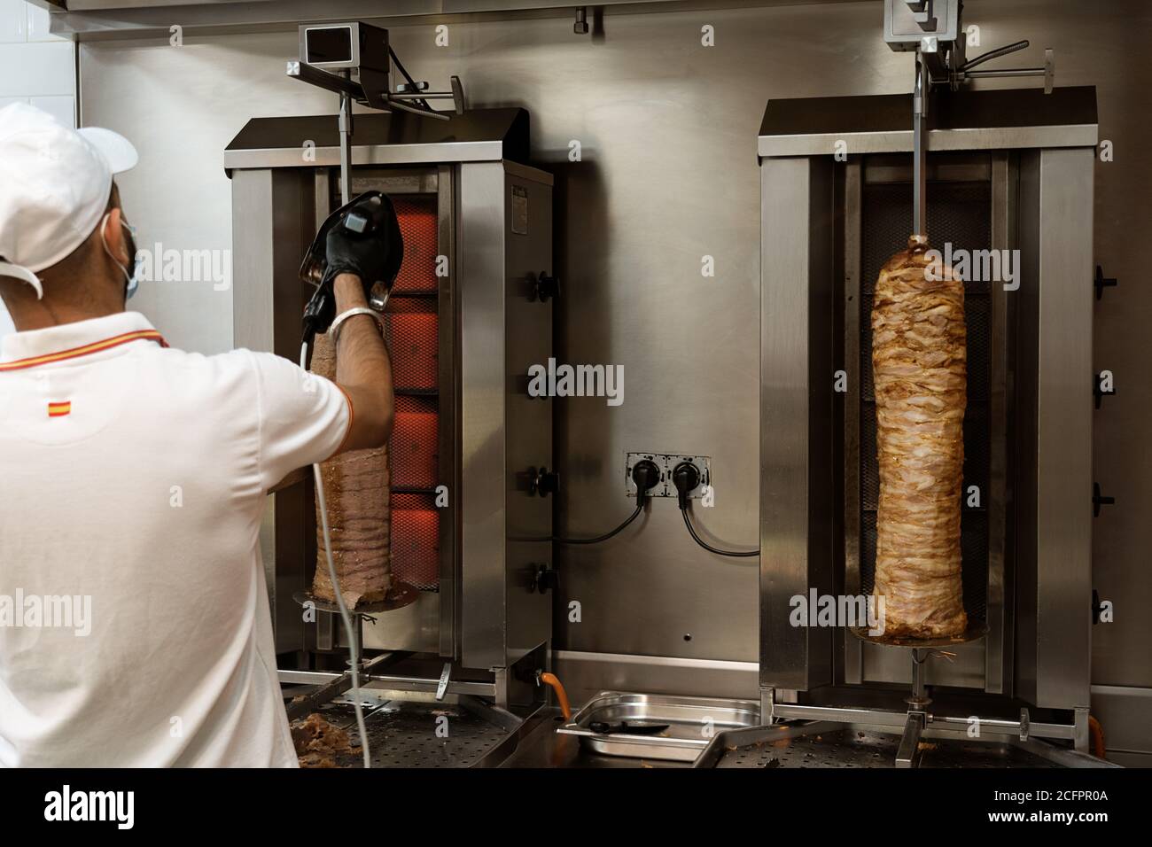 Uniformed chef, cutting and preparing chicken and beef doner kebabs ...