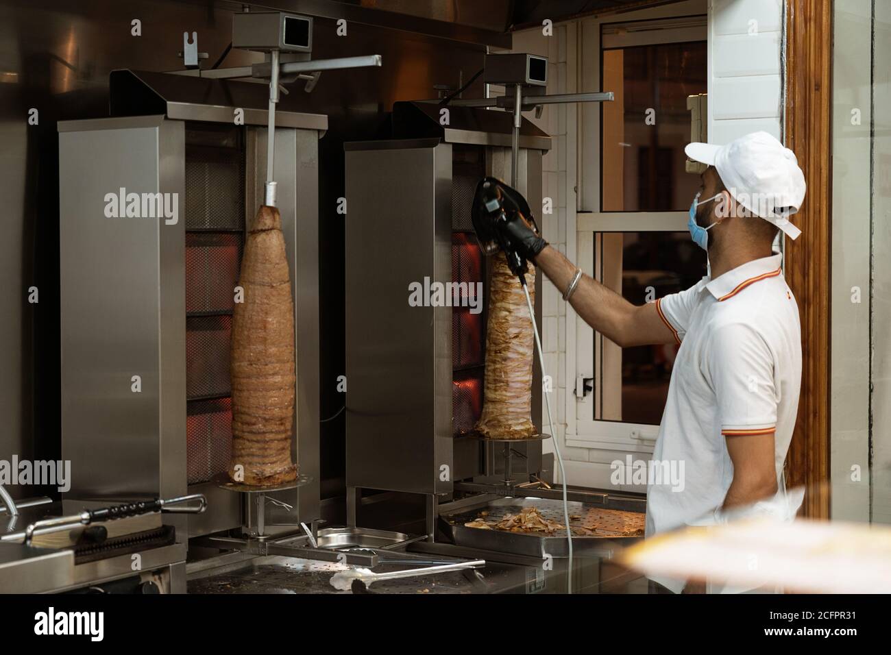 Uniformed chef, cutting and preparing chicken and beef doner kebabs ...