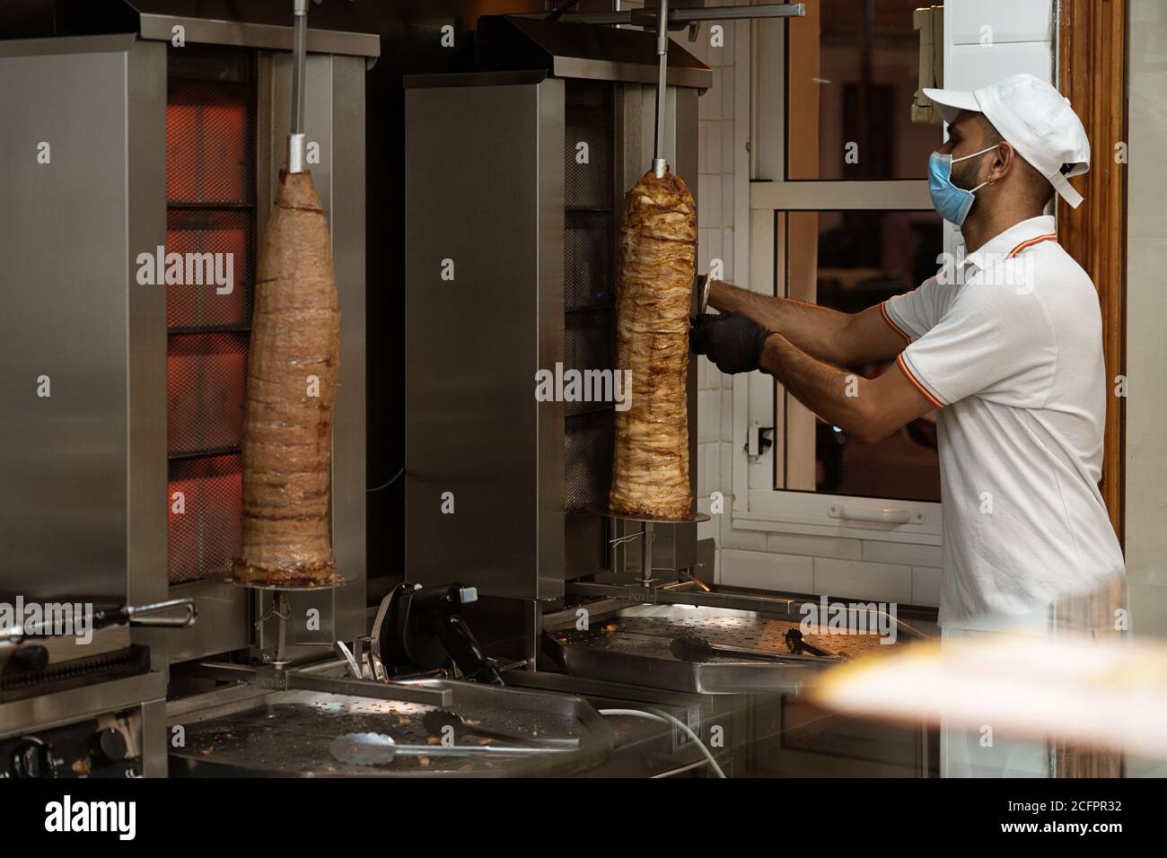 Uniformed chef, cutting and preparing chicken and beef doner kebabs ...