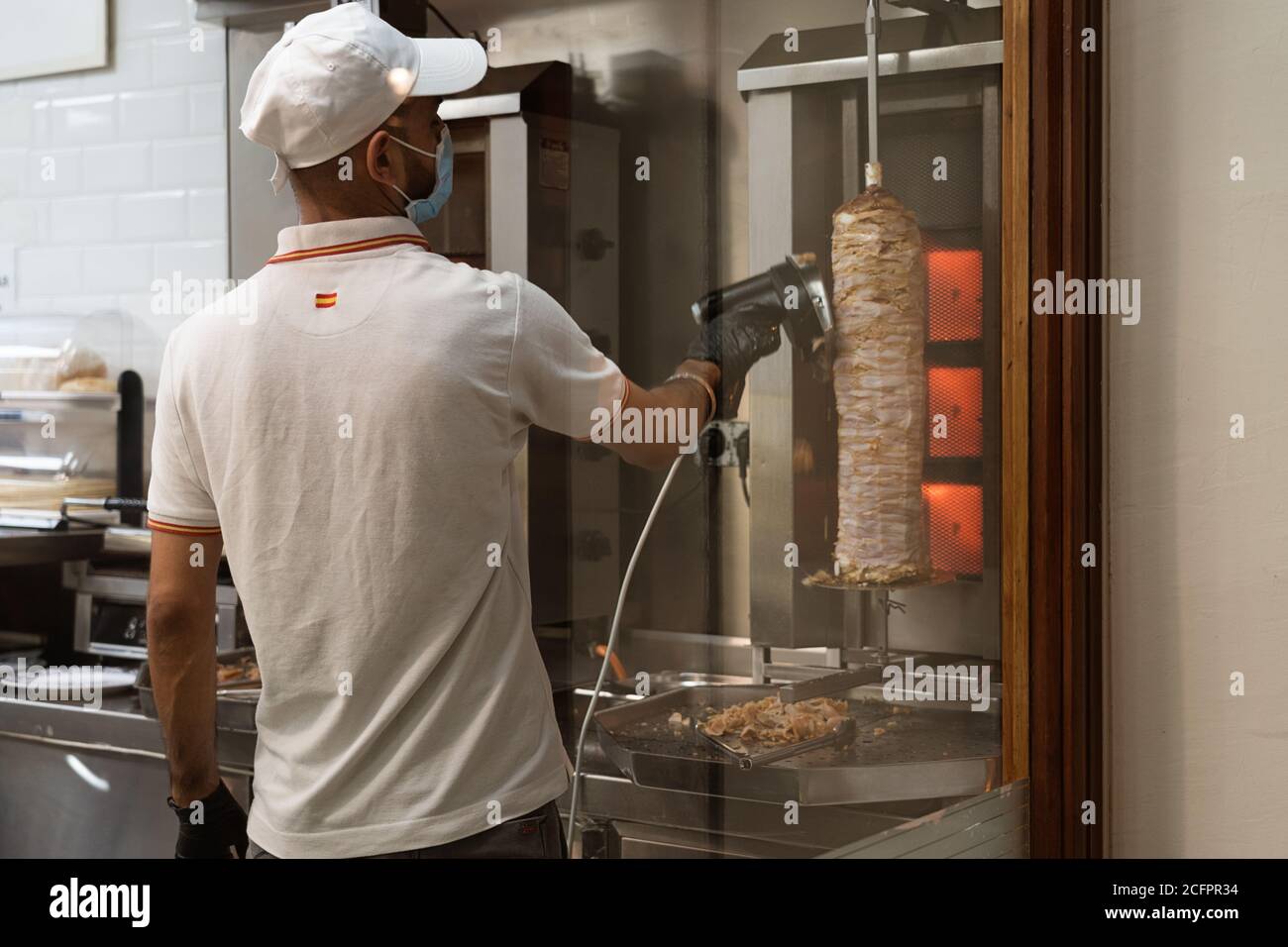 Uniformed chef, cutting and preparing chicken and beef doner kebabs ...
