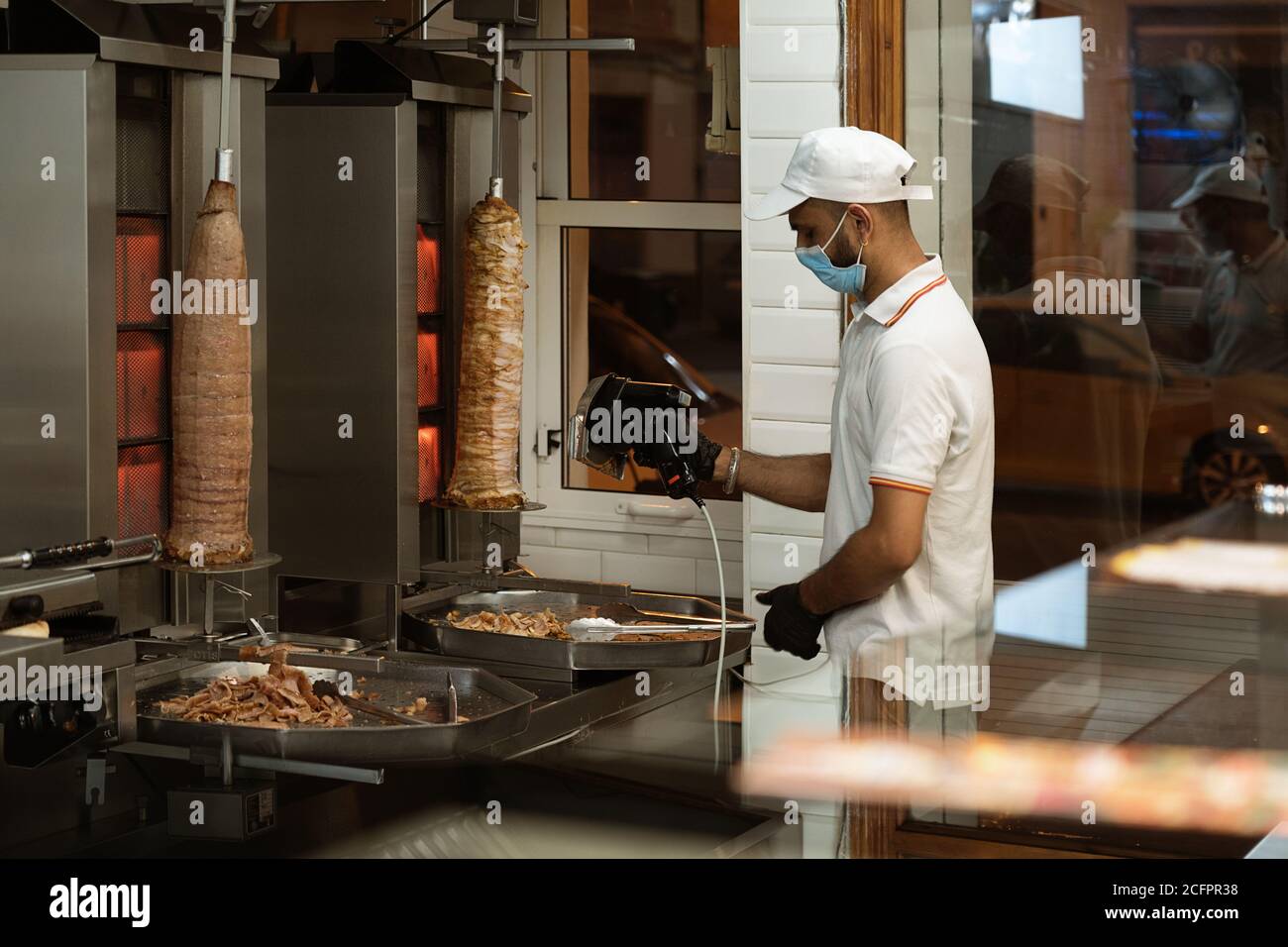 Uniformed chef, cutting and preparing chicken and beef doner kebabs ...