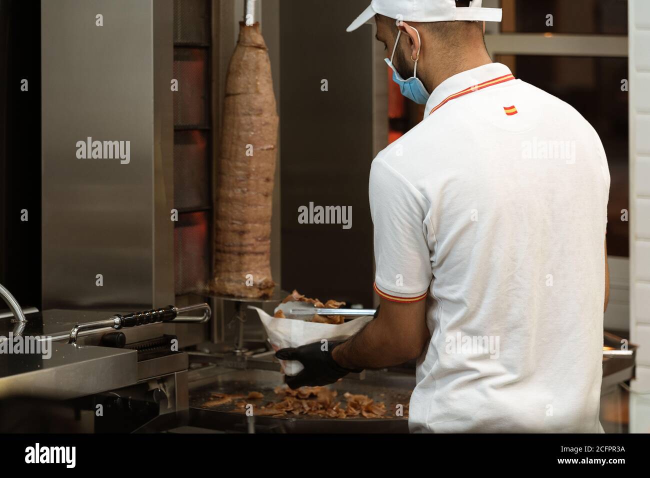 Uniformed chef, cutting and preparing chicken and beef doner kebabs ...