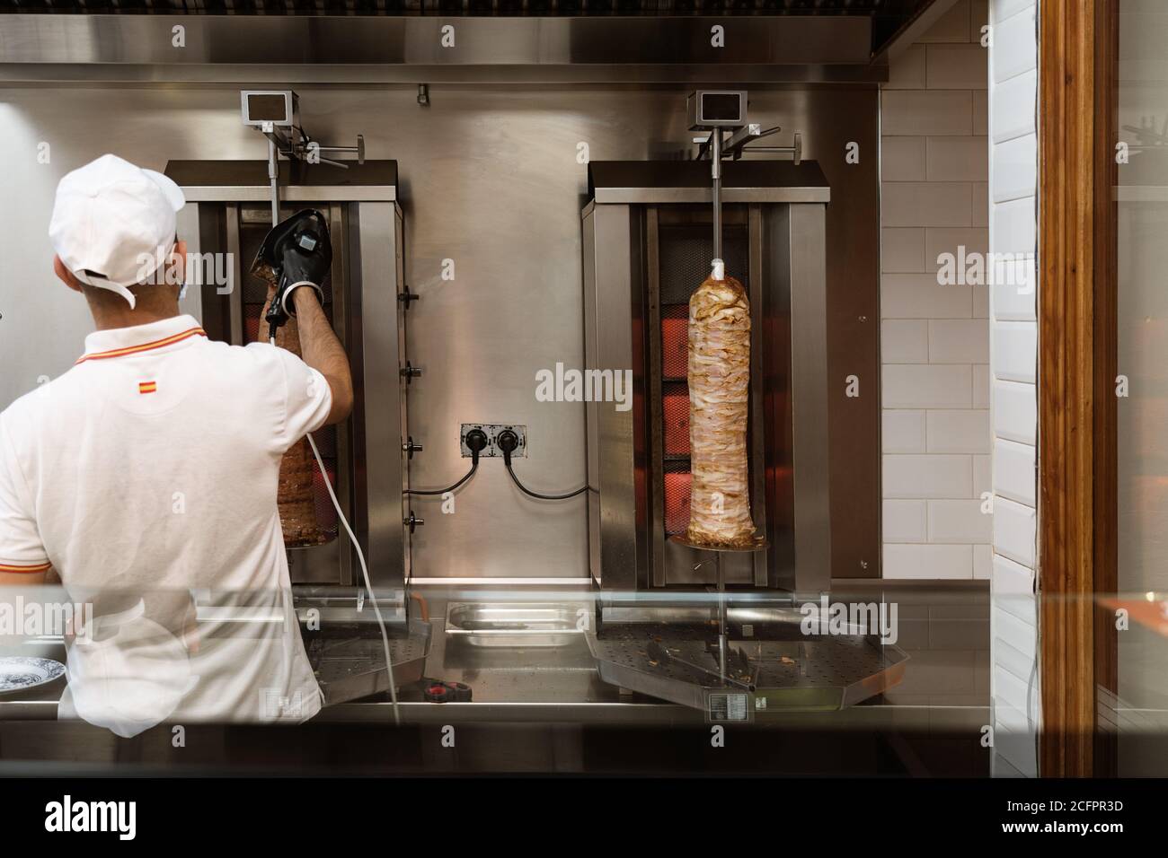 Uniformed chef, cutting and preparing chicken and beef doner kebabs ...