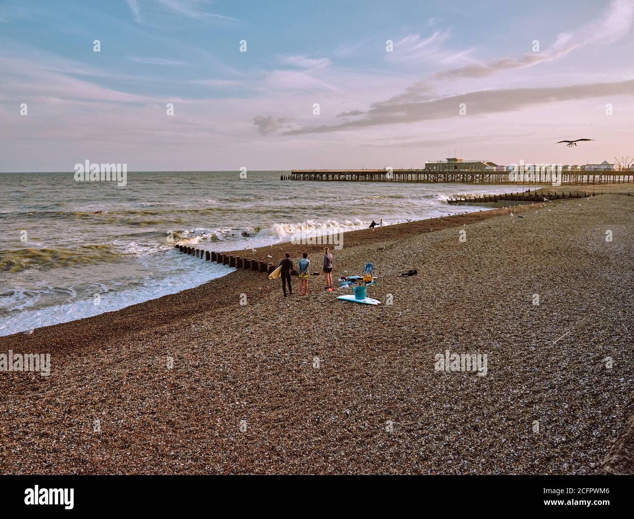 Visitors enjoying the late sun and Hastings Pier and shingle beach at ...