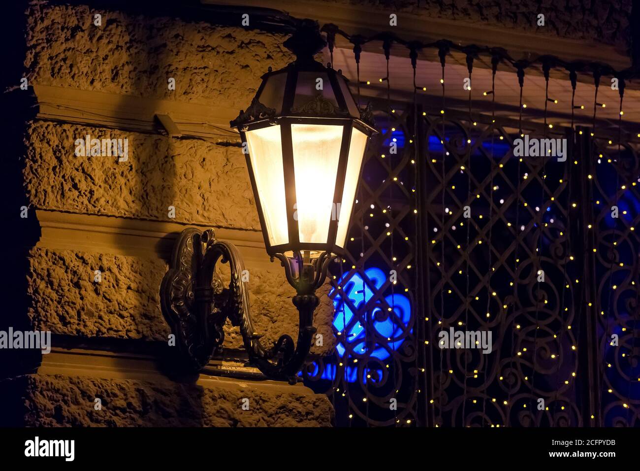 black wrought iron lantern with frosted glass shines with warm light on ...