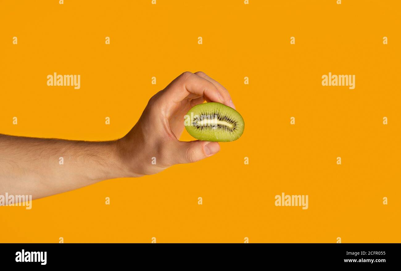 Male hand holding cut ripe kiwi fruit over orange background Stock ...