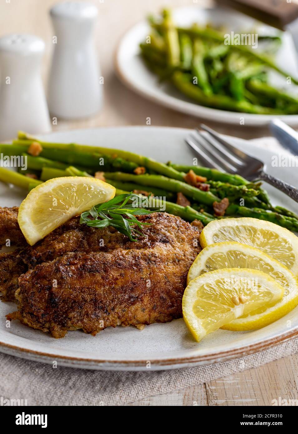 Baked tilapia fish fillets with sliced lemons and asparagus on a dinner ...