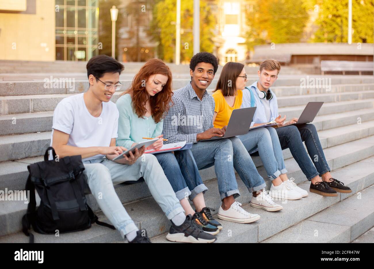 Multiethnic Students Learning Together Using Gadgets Sitting On Steps ...