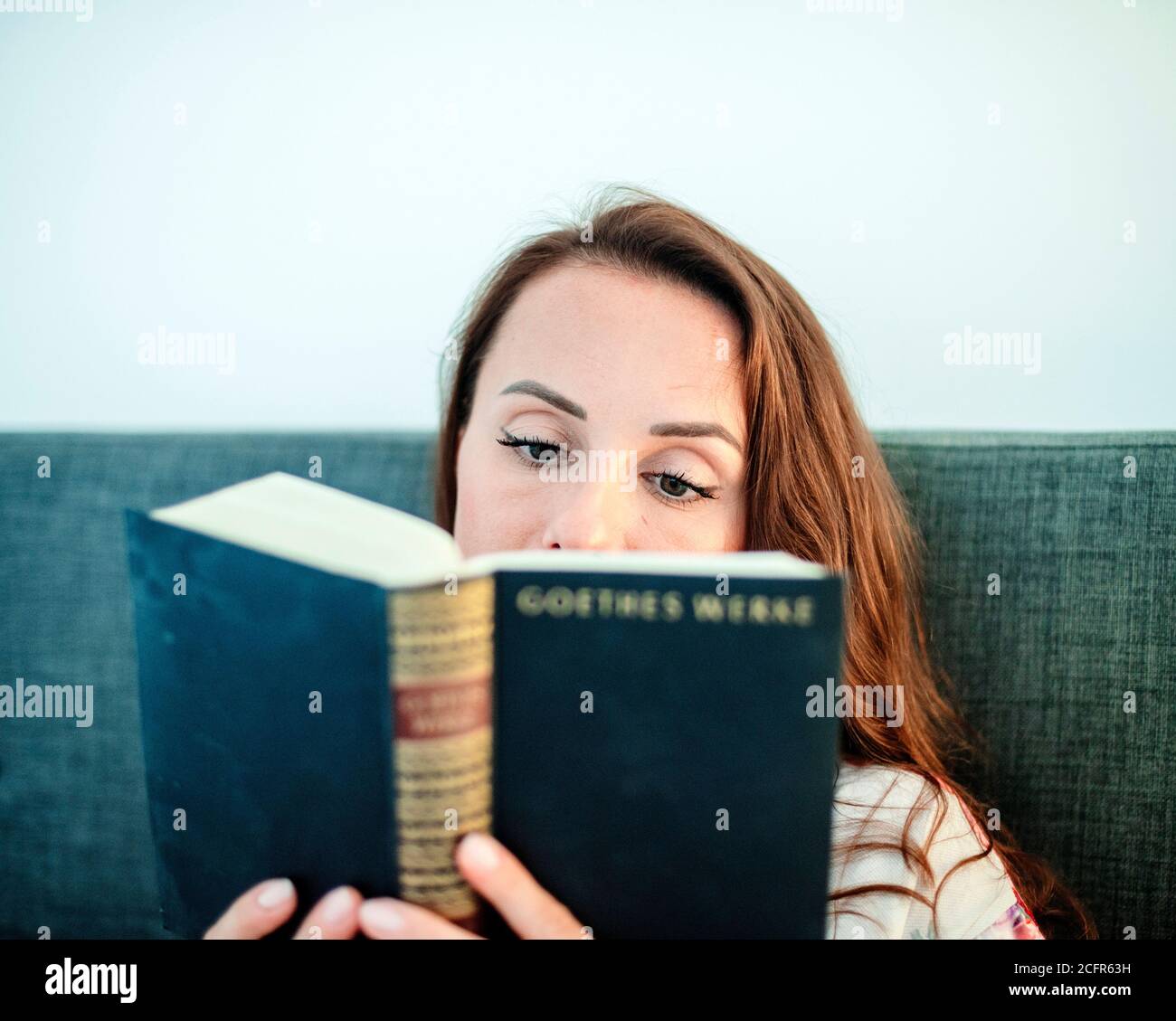 Woman reading a book on a couch Stock Photo - Alamy