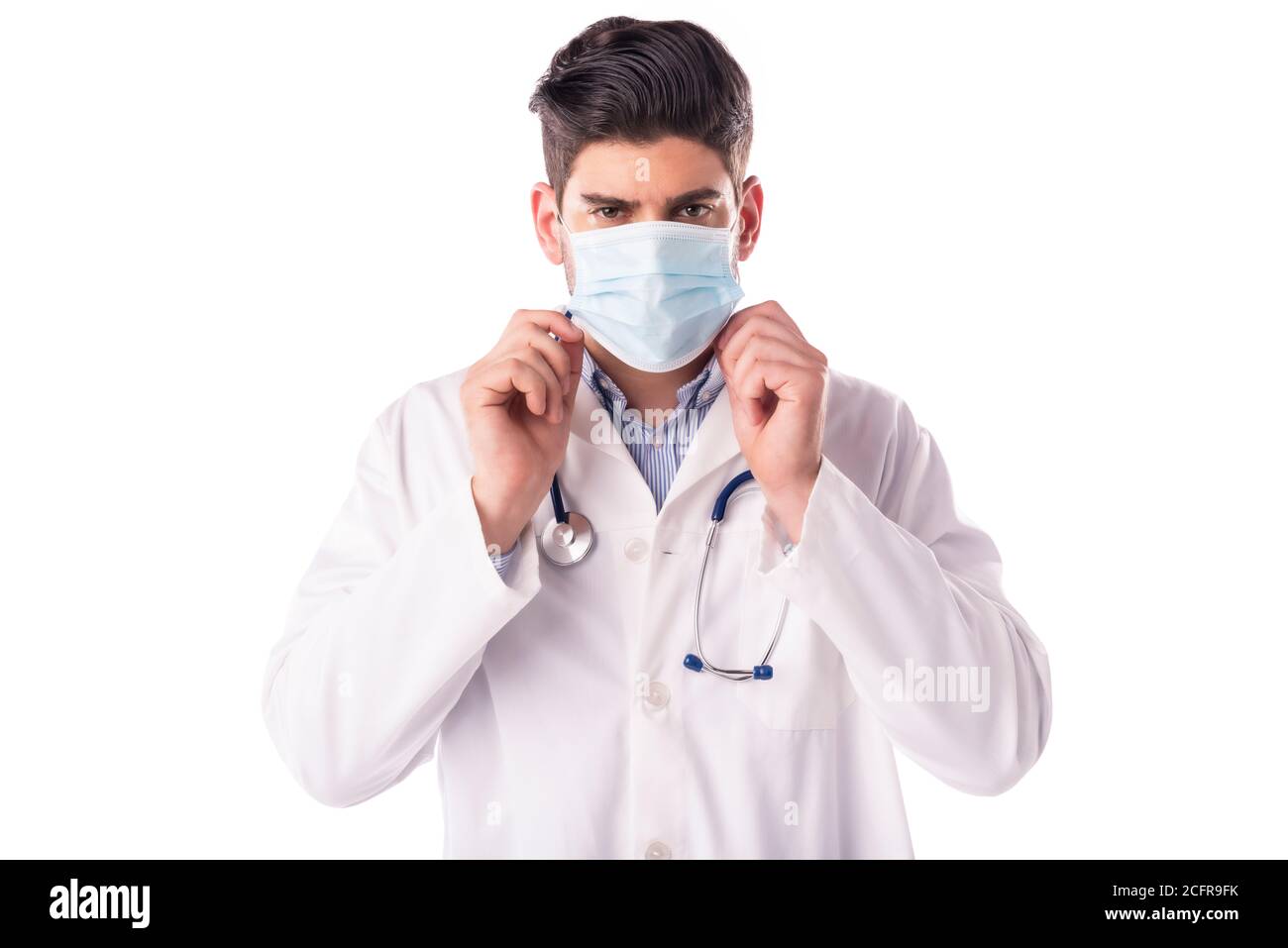 Shot of male doctor putting on face mask while standing at isolated ...