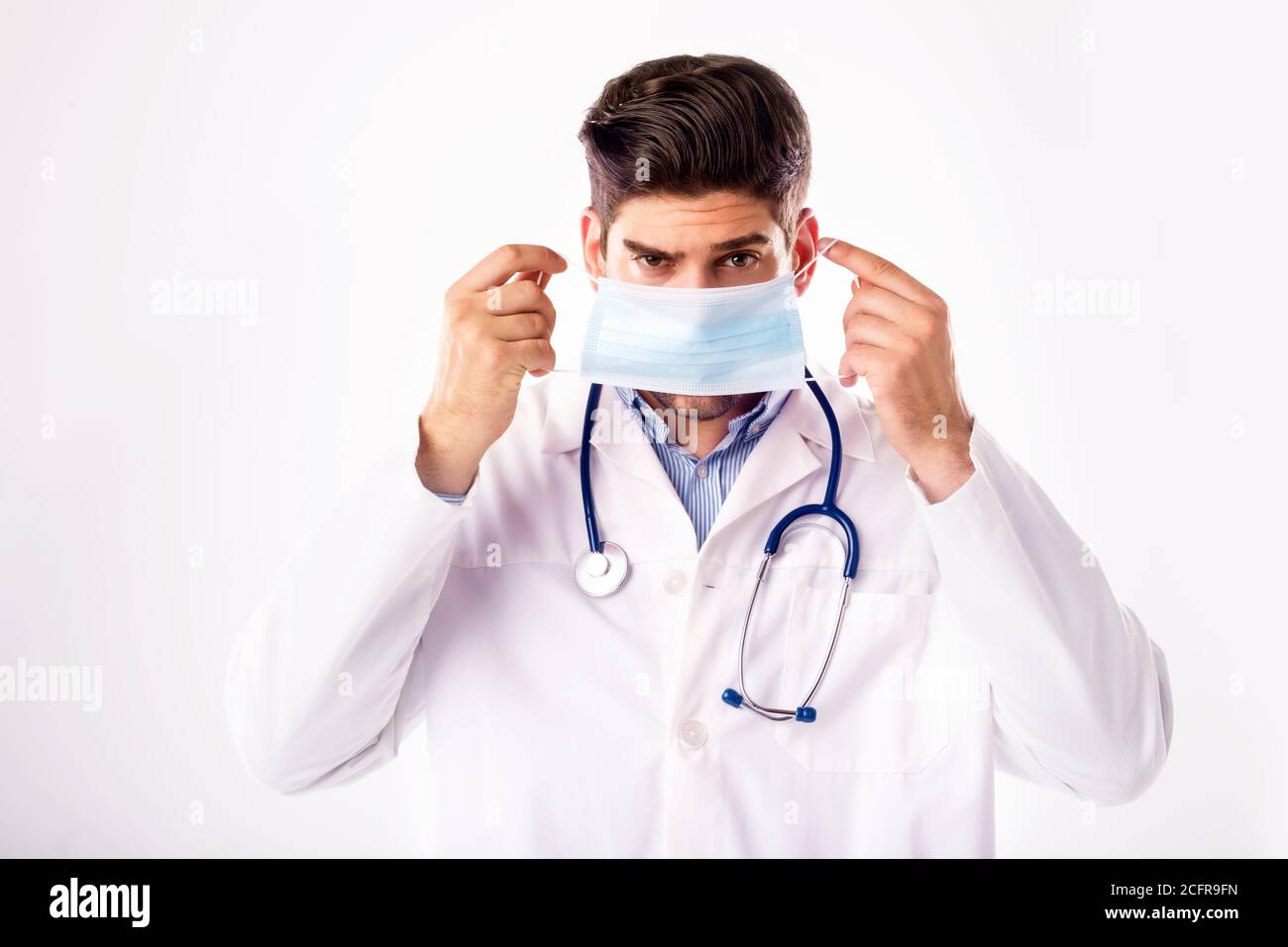 Shot of male doctor putting on face mask while standing at isolated ...