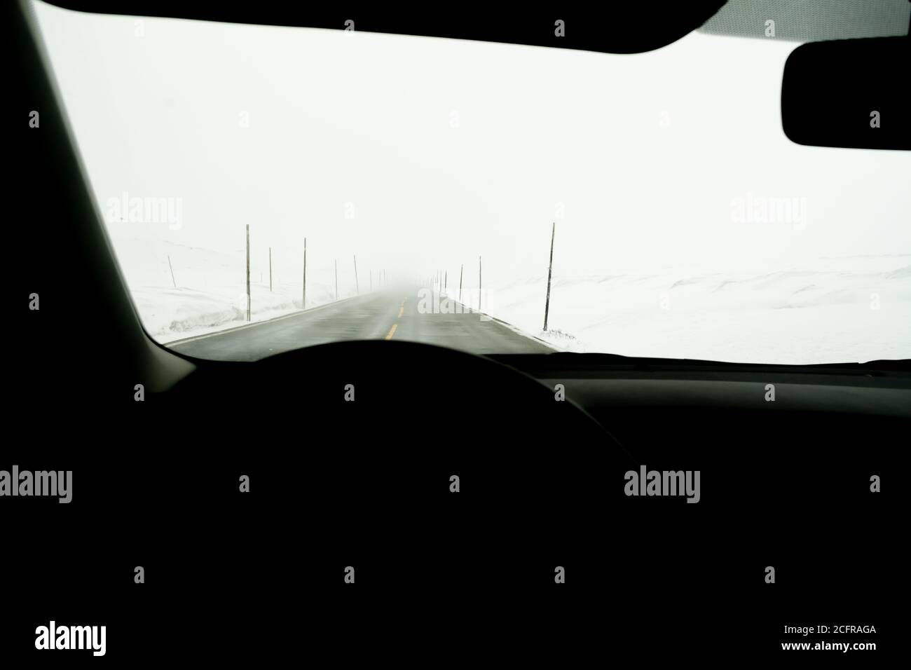 Car interior point of view on road cleared from snow and ice, but piled ...