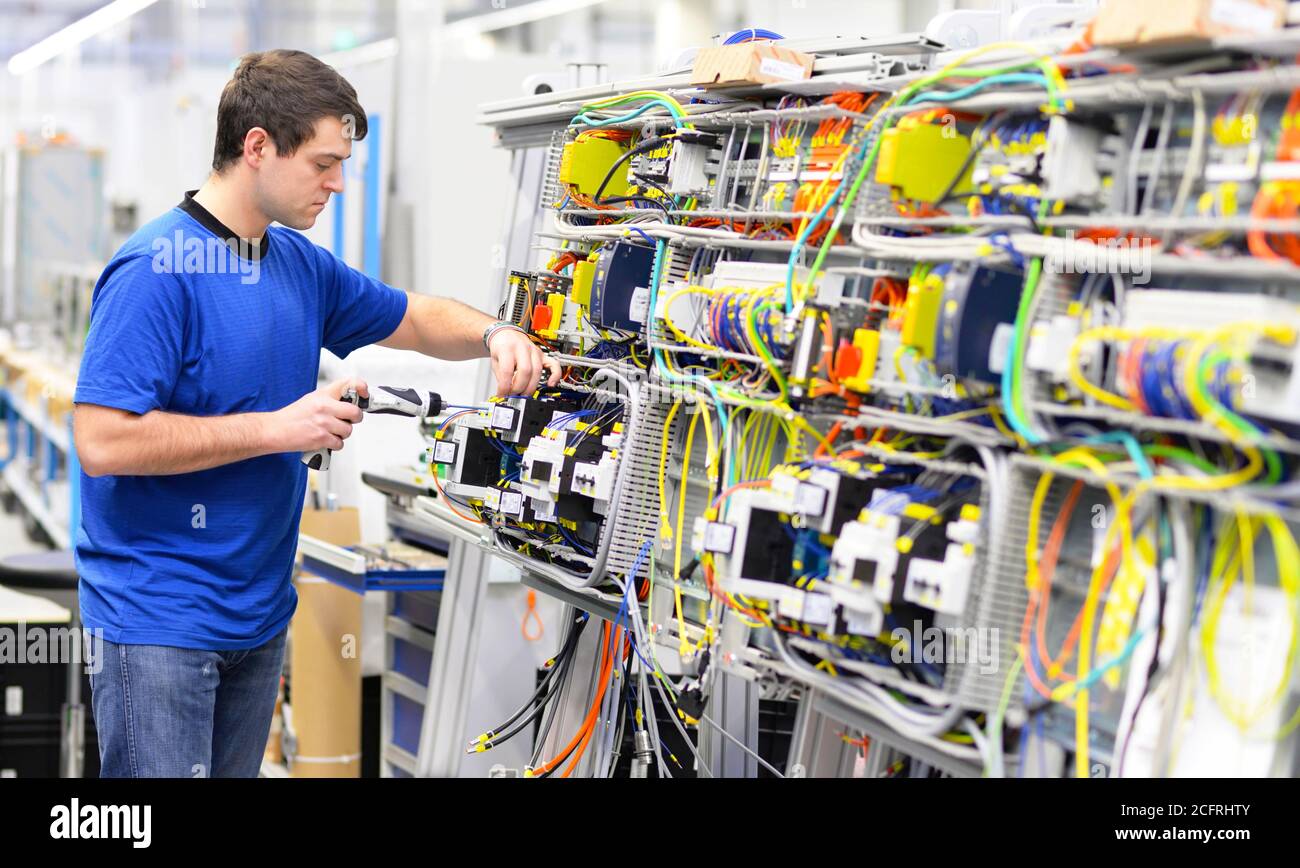 young apprentice assembles components and cables in a factory in a ...