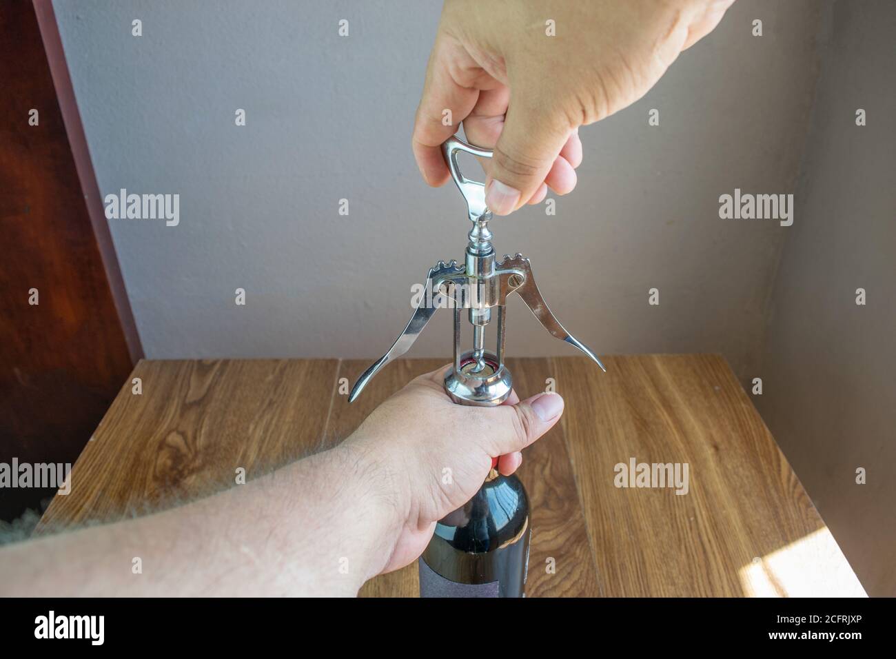 personal perspective of man uncorking bottle of red wine with corkscrew ...