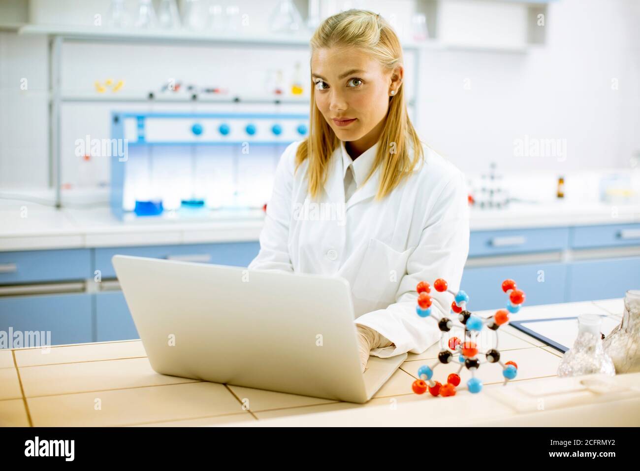 Cute female researcher in white lab coat using laptop while working in ...