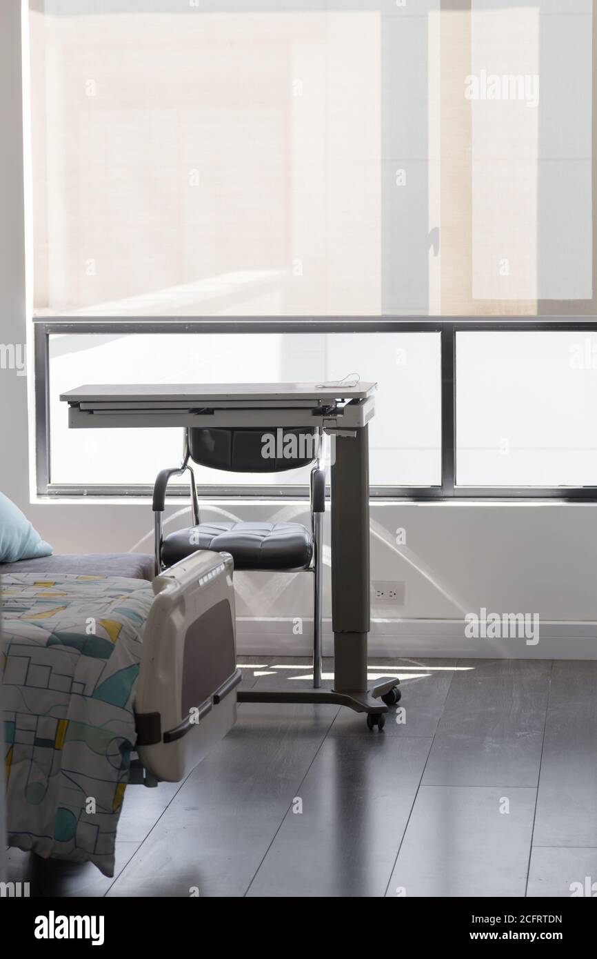 white clinic room, with a large window next to a movable table, a chair ...