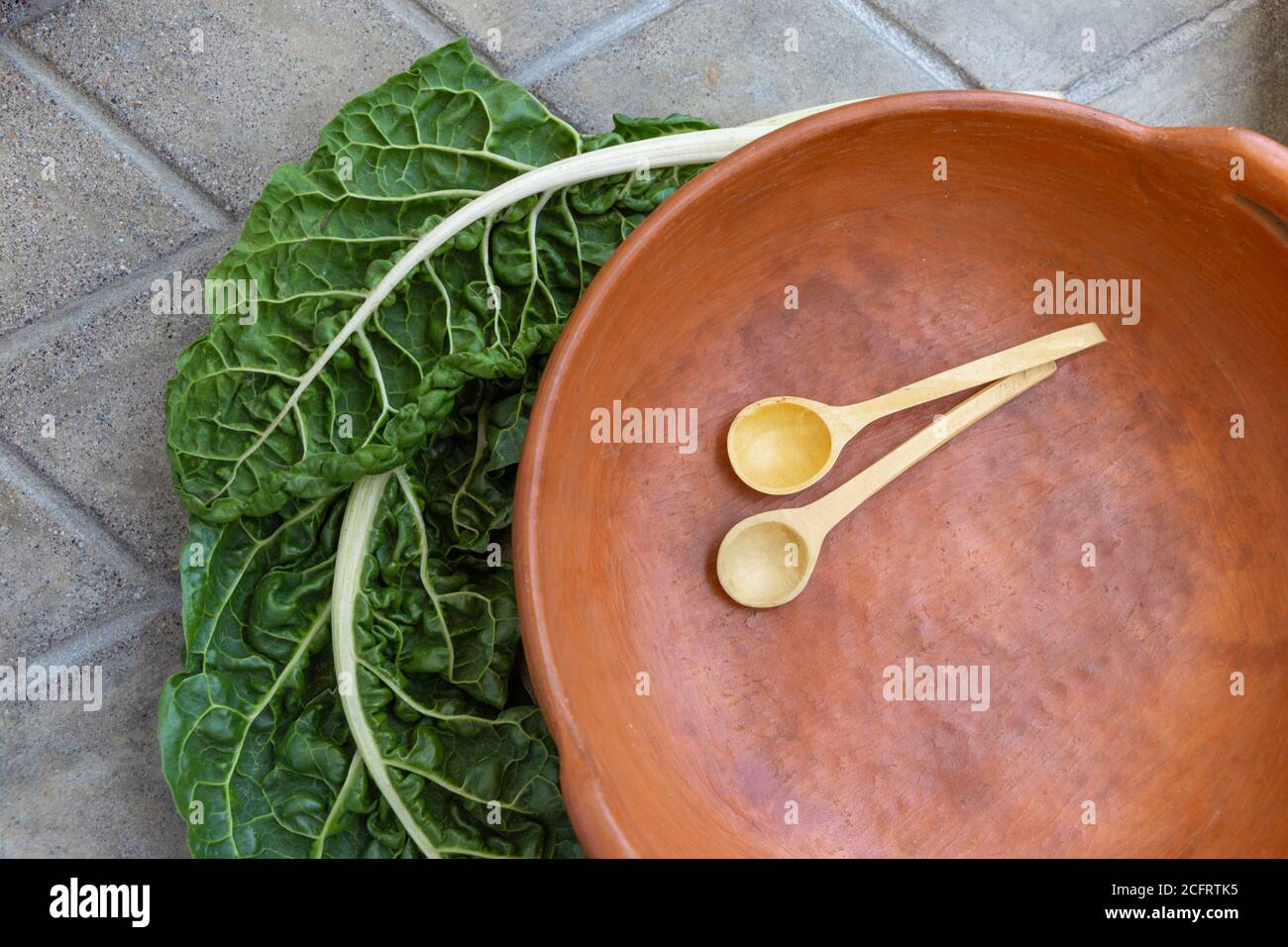 ceramic pan with stick spoons inside, winged spinach leaves on tile ...