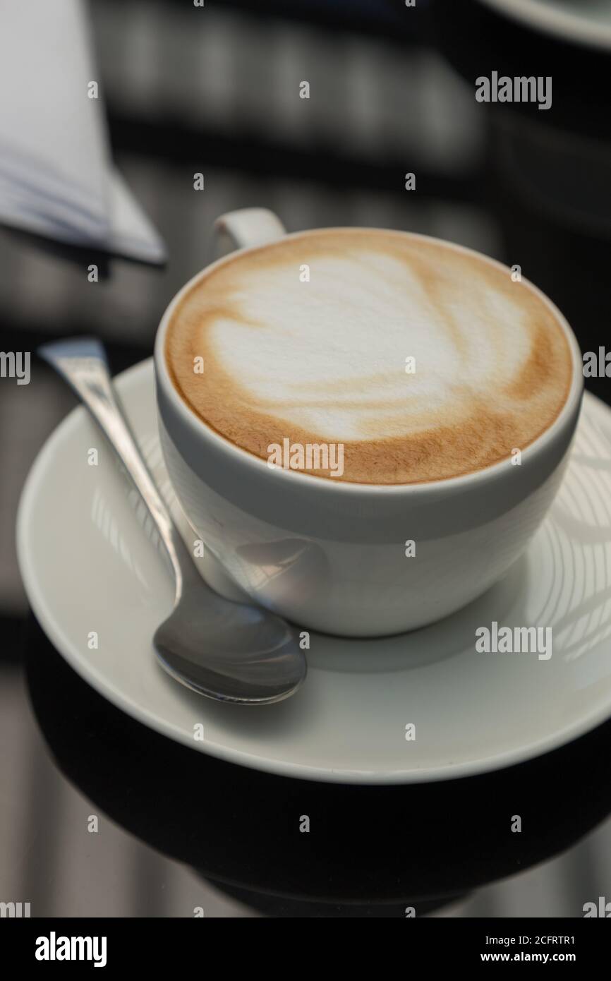 small white cup with a design in the coffee foam with a plate, spoon ...