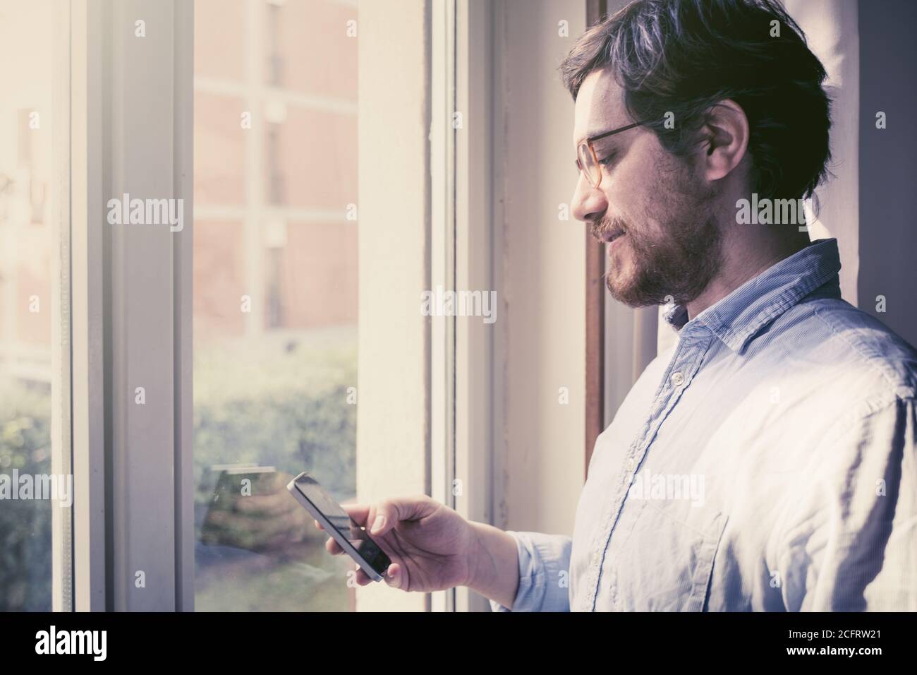 Guy holding cellphone at home next to the window Stock Photo - Alamy