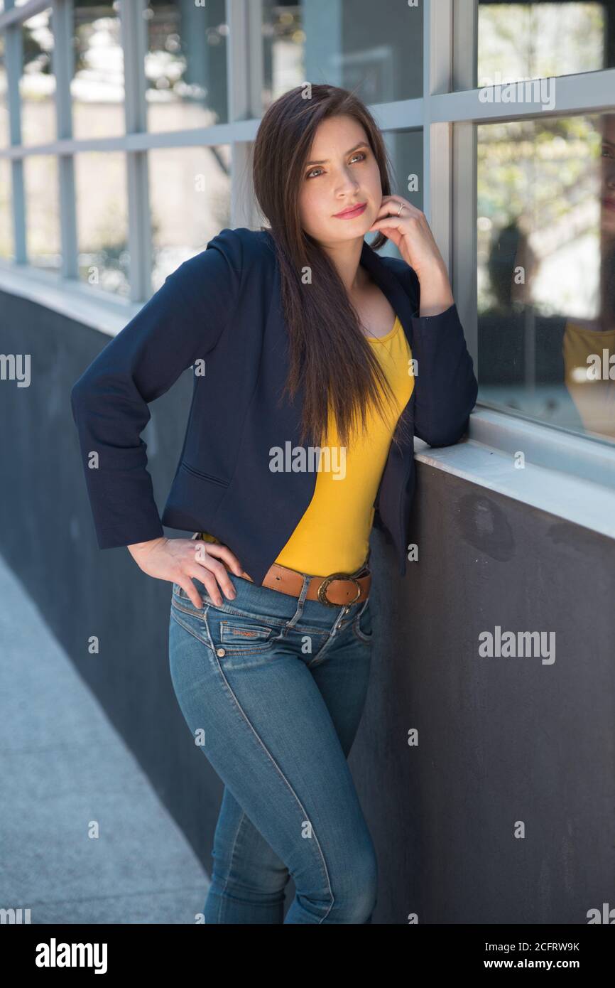 Latin white skinned woman with long hair, posing standing by a window ...