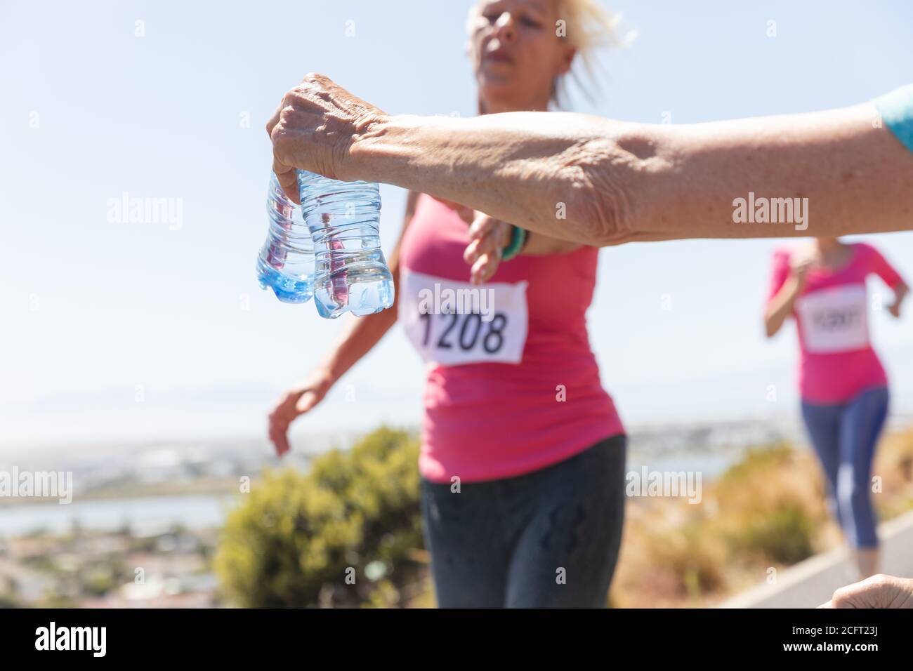 Mid section of woman giving water bottles to female runners Stock Photo ...