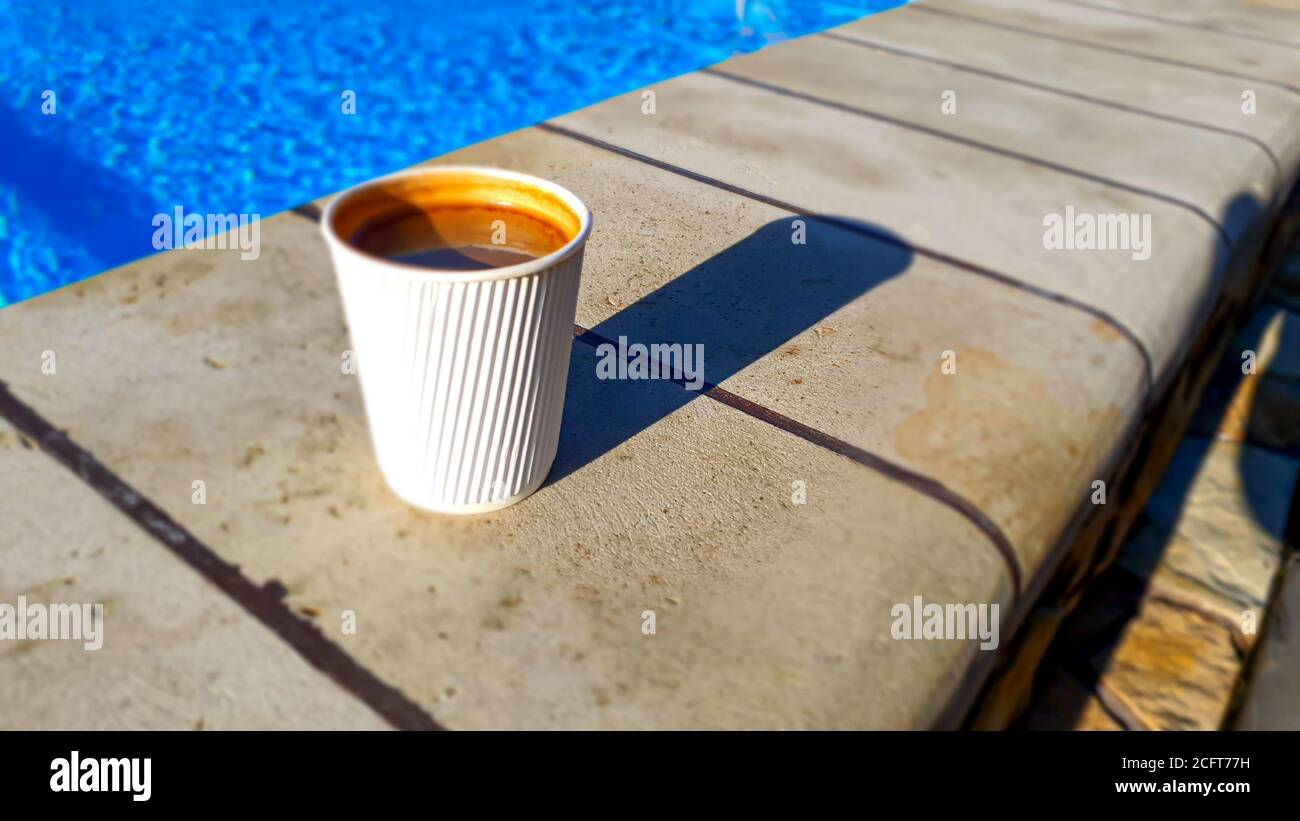 Coffee in a disposable glass and a glass cup by the pool. Cheerful ...