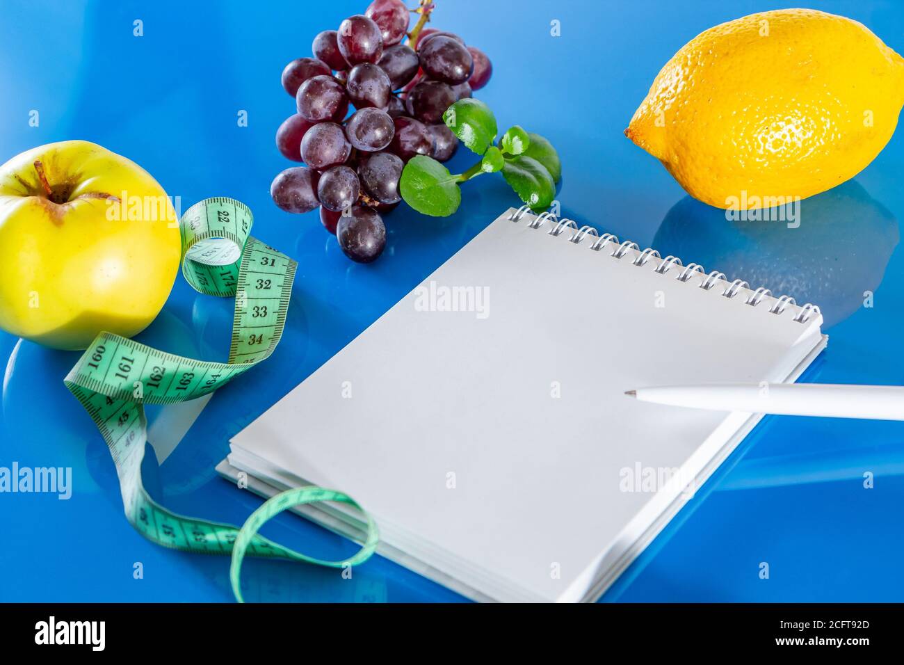 Blank notebook, fruits and measuring tape on a blue background. The ...