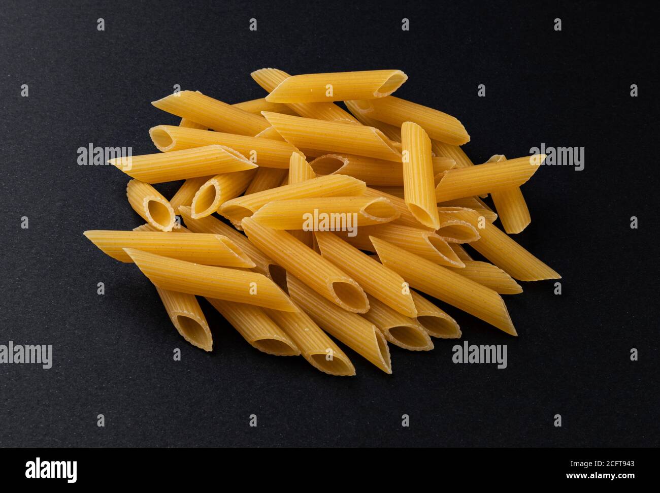 Raw penne rigate pasta isolated on black background Stock Photo - Alamy