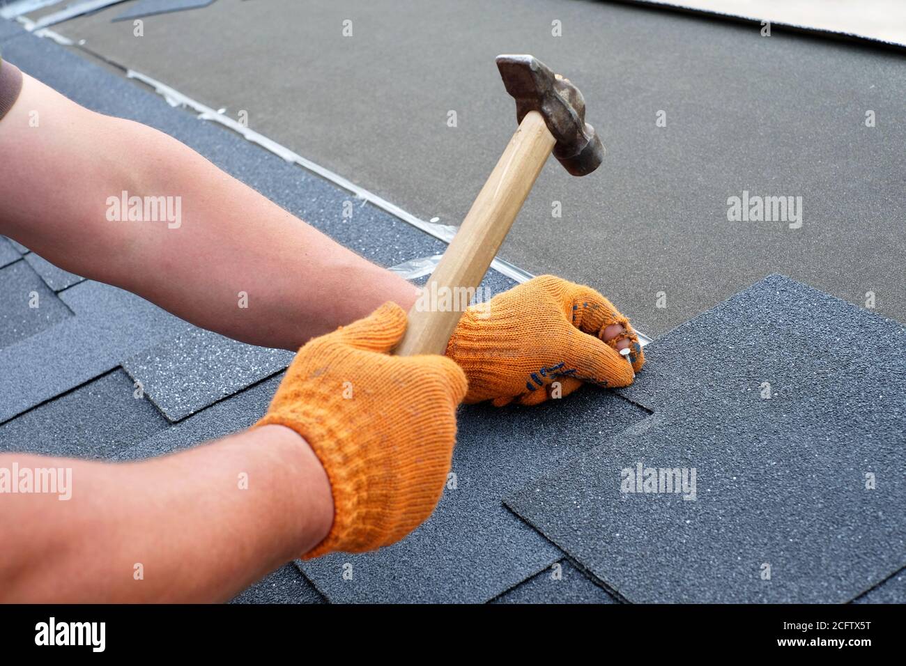 Roofer hands installing bitumen roof shingles using hammer in nails ...