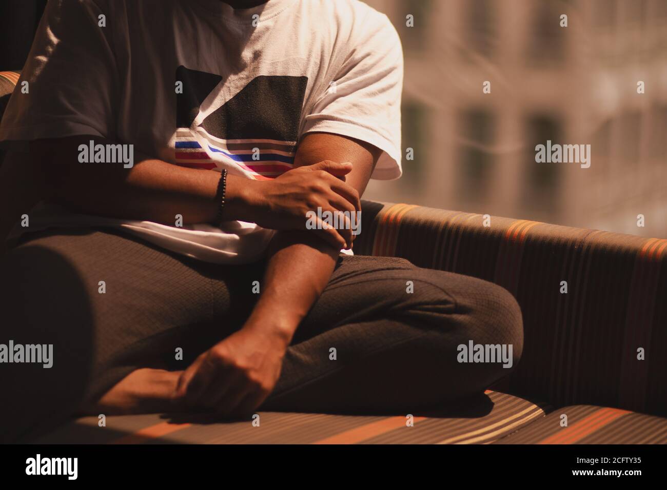 African male sitting next to a window holding his arm with his hand ...