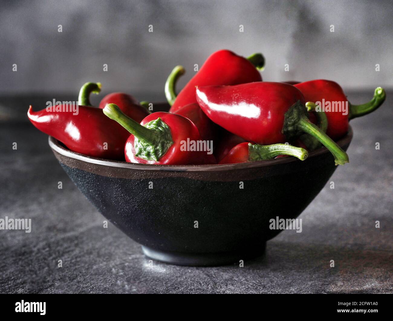 Red hot chilli peppers in black bowl on table. Blurry background with ...
