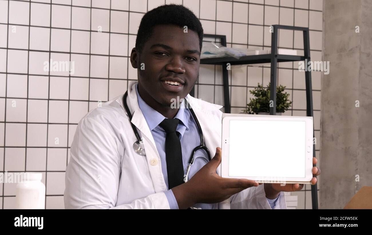 Handsome serious African doctor presenting product on tablet screen ...