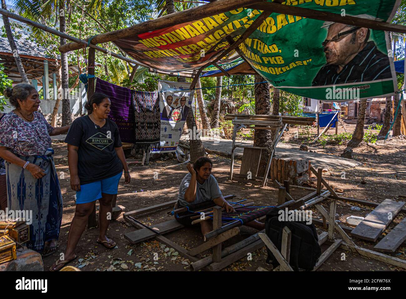 Women with looms under an awning with election campaign slogans, Sunda ...